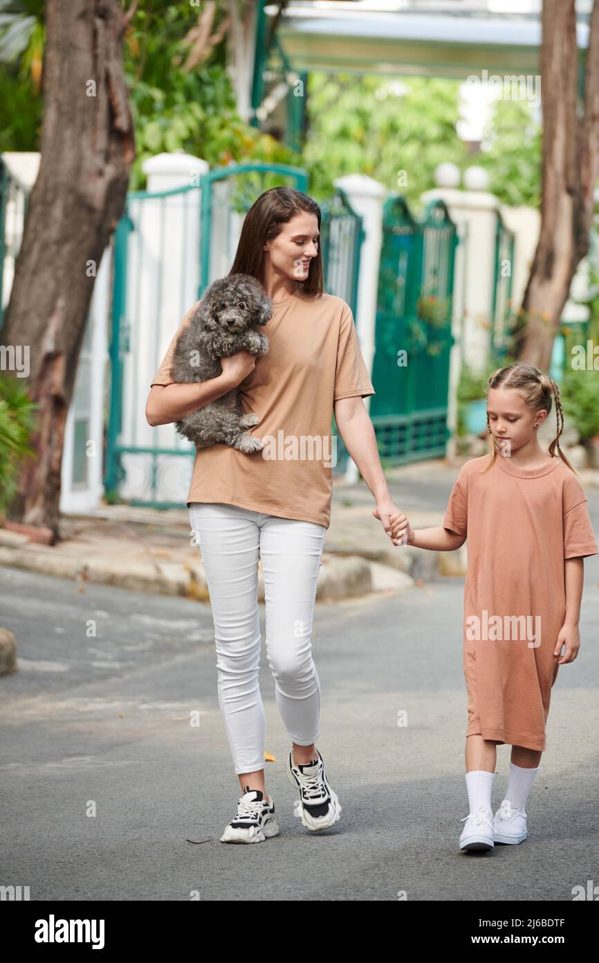 Woman carrying small dog when walking outside with preteen daughter ...