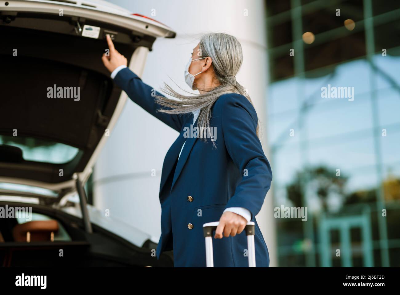 Grey asian woman in face mask opening trunk by airport outdoors Stock ...