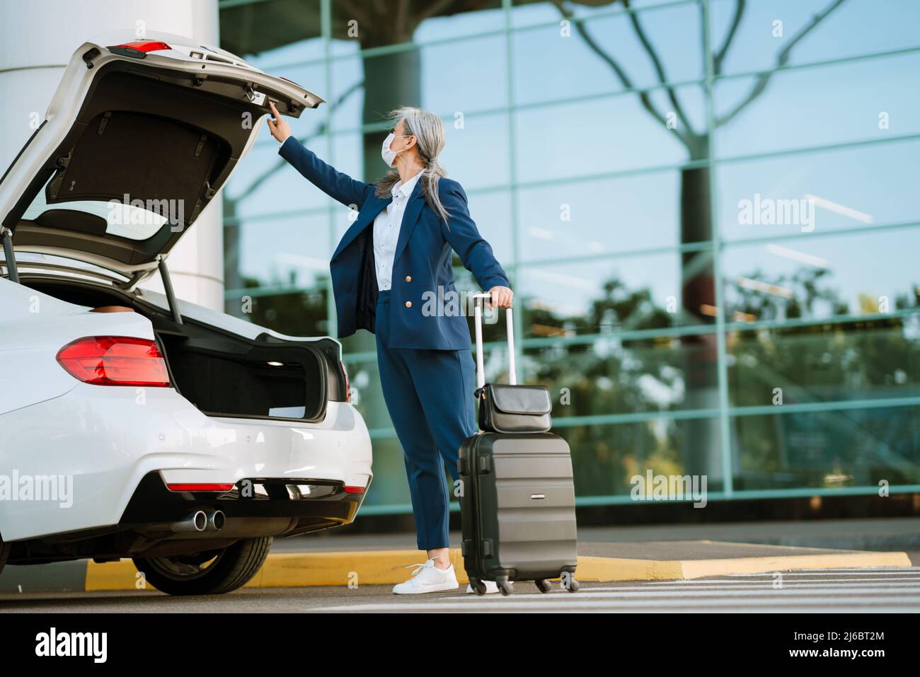 Grey asian woman in face mask opening trunk by airport outdoors Stock ...