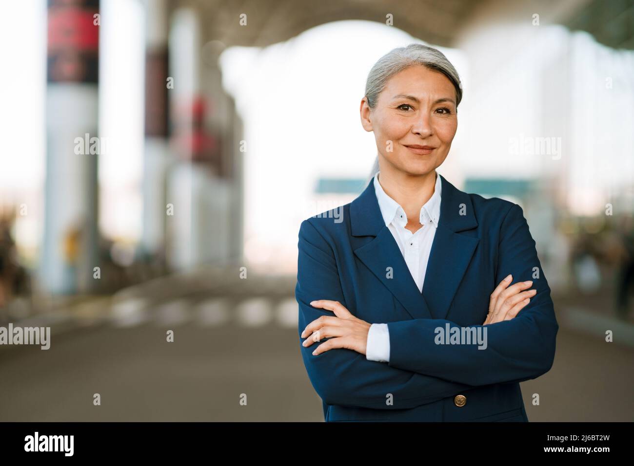 Grey asian woman in jacket smiling while posing on airport parking ...