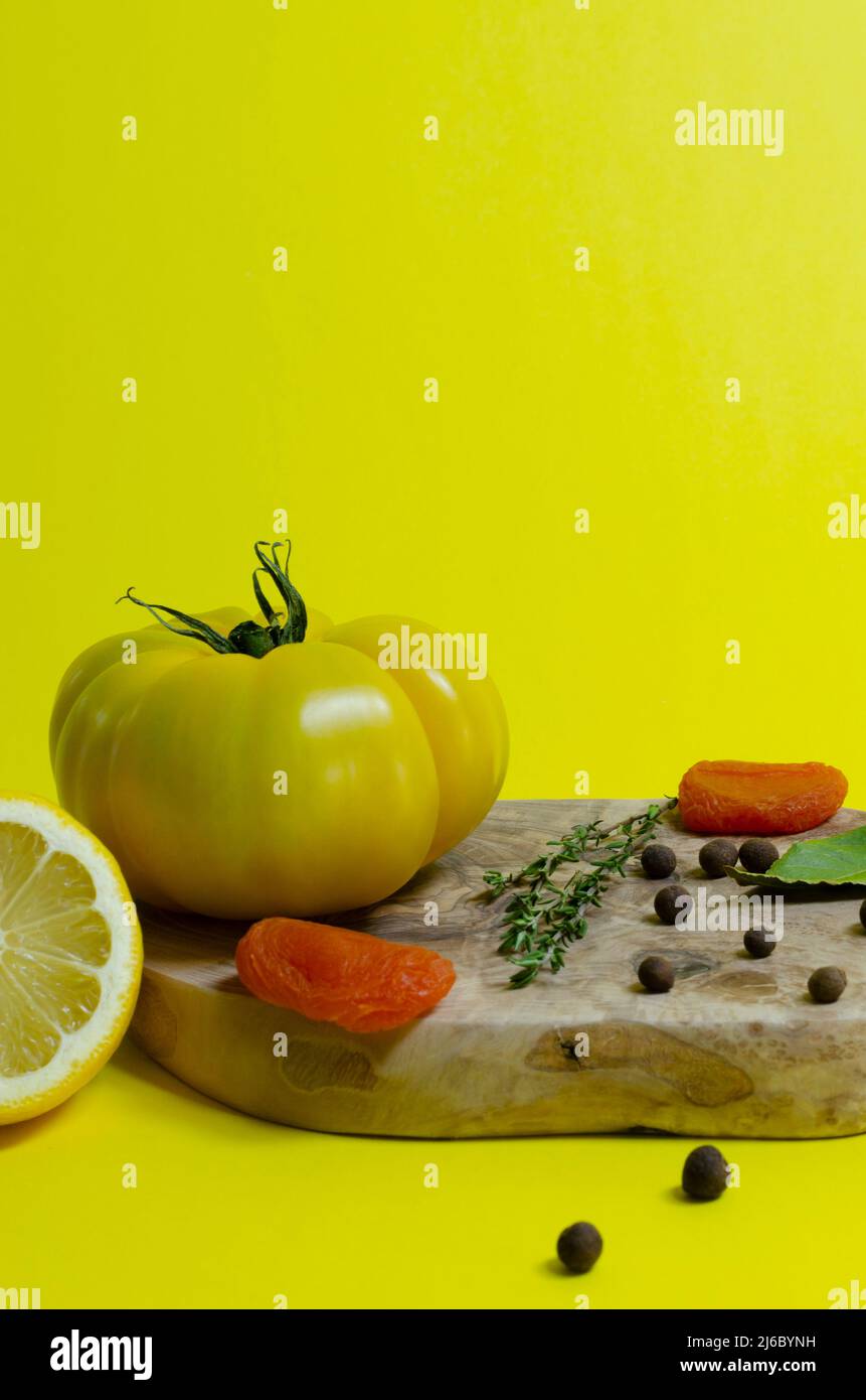 Yellow tomato, lemon, peppercorns, bay leaves, and dried apricots lie ...
