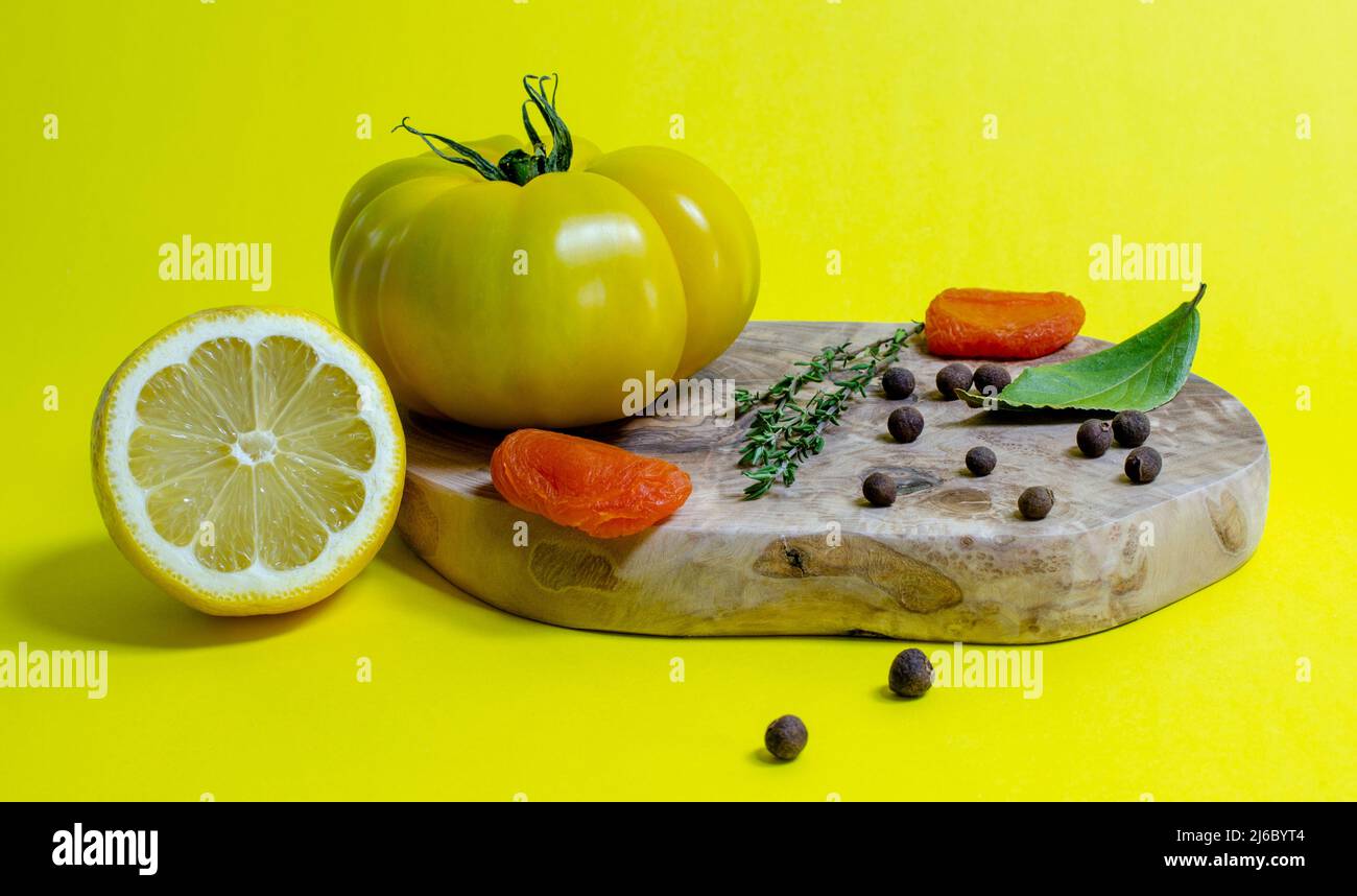 Yellow tomato, lemon, peppercorns, bay leaves, and dried apricots lie ...