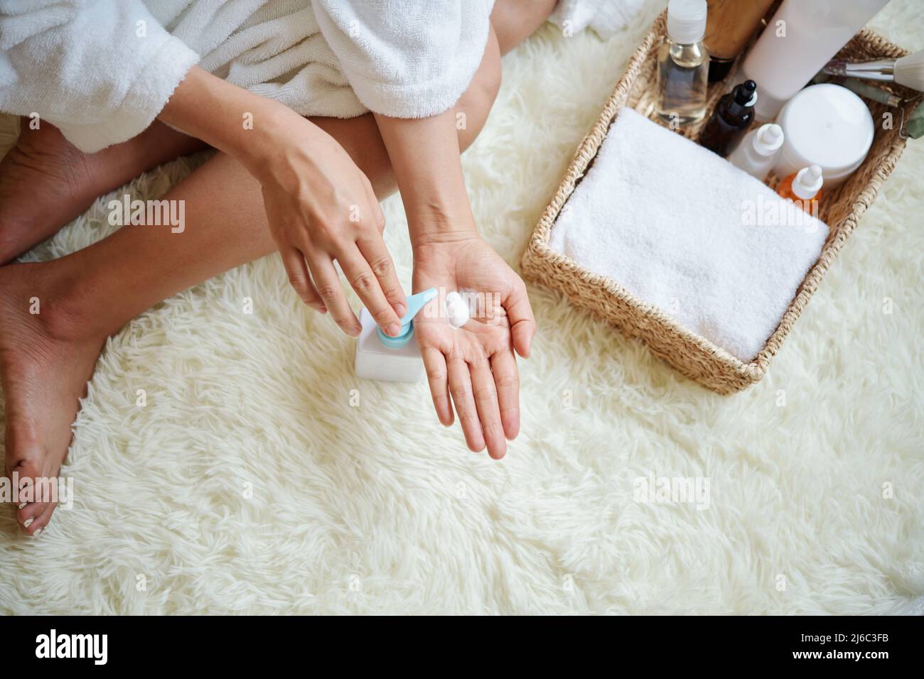 Woman pumping moisturizing body lotion in hand to apply after shower ...