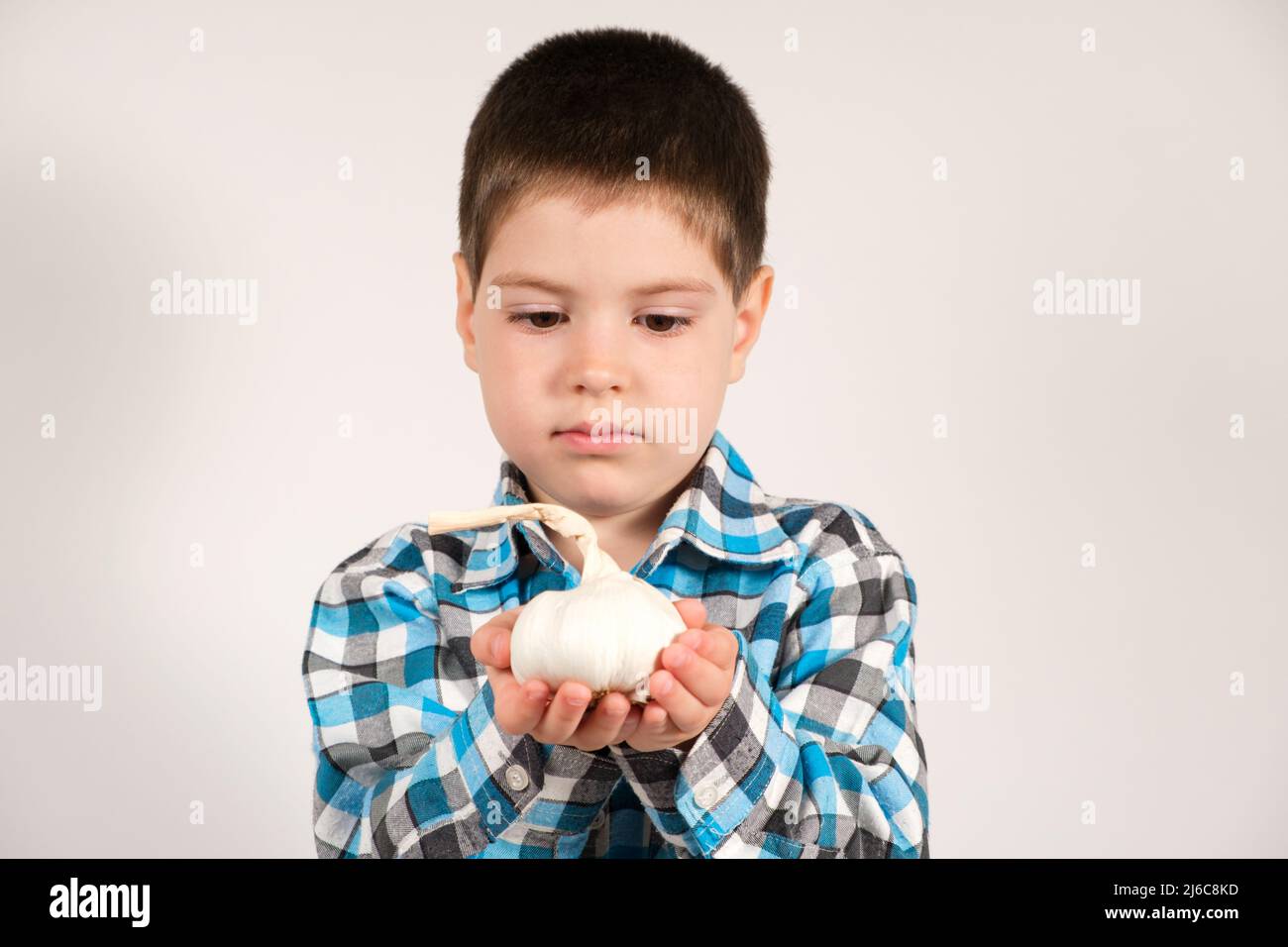 A 4-year-old preschool boy holds garlic on a white background ...