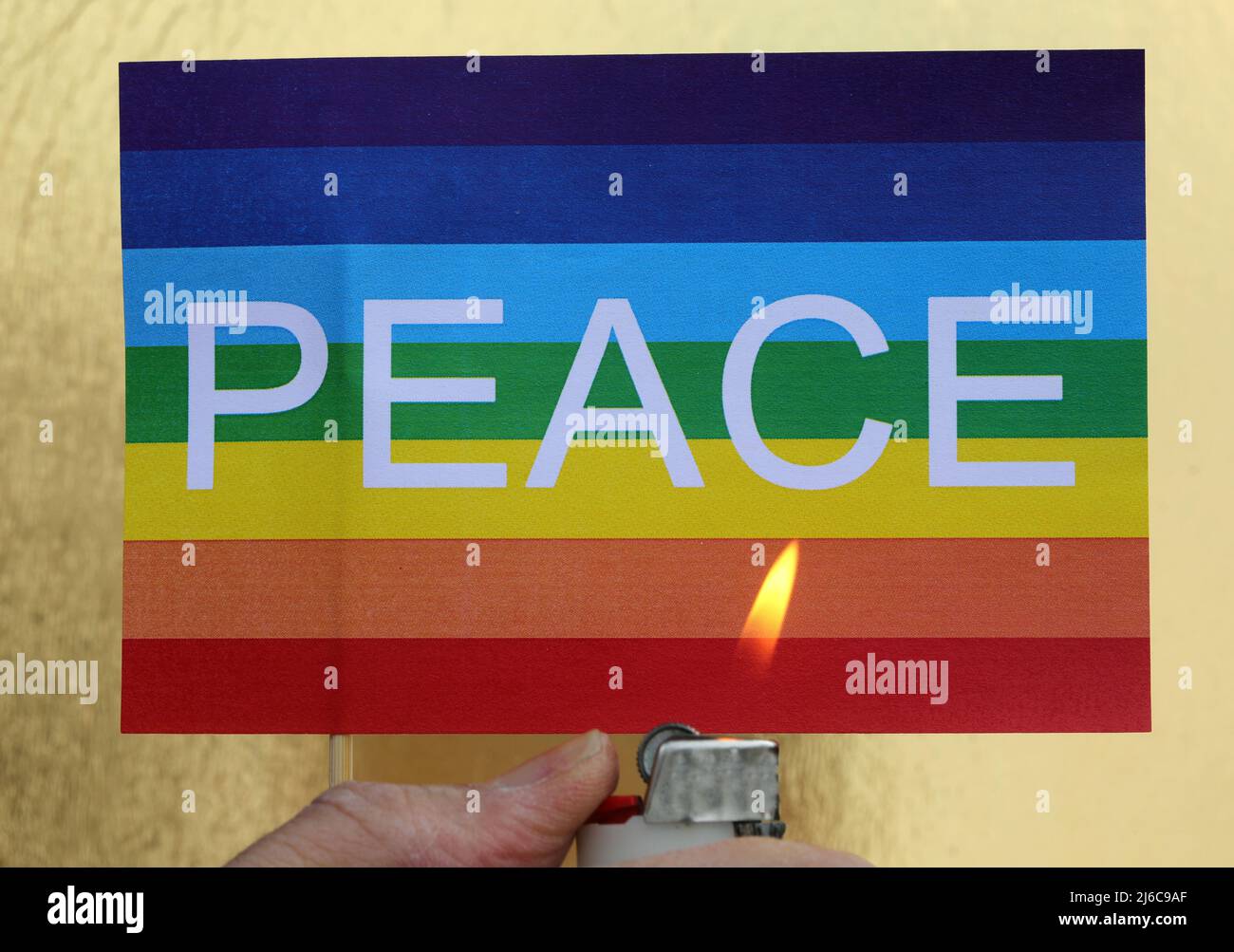 hand with lighter and fire burning multicolored flag with text PEACE ...