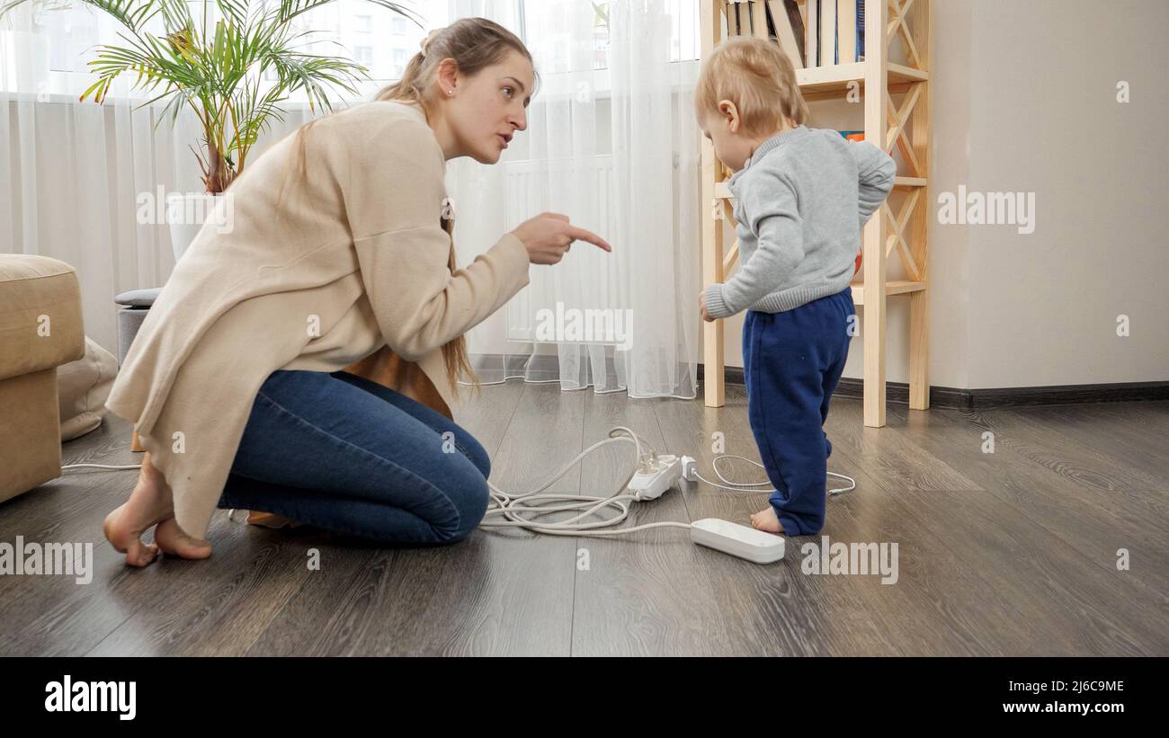 Young caring mother telling her baby son not to play with electricity ...