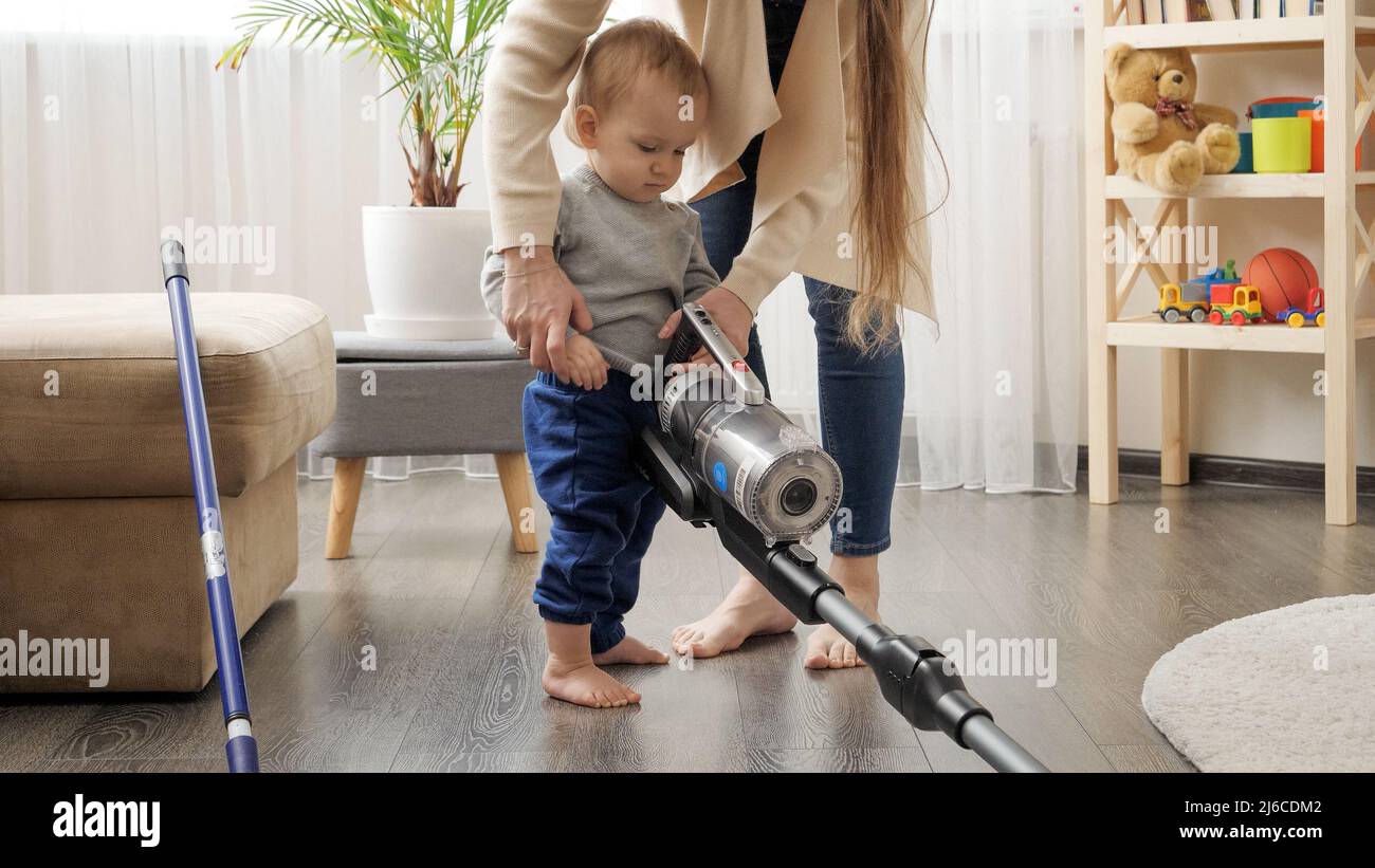 Young mother doing housework teaching and giving vacuum cleaner to her ...