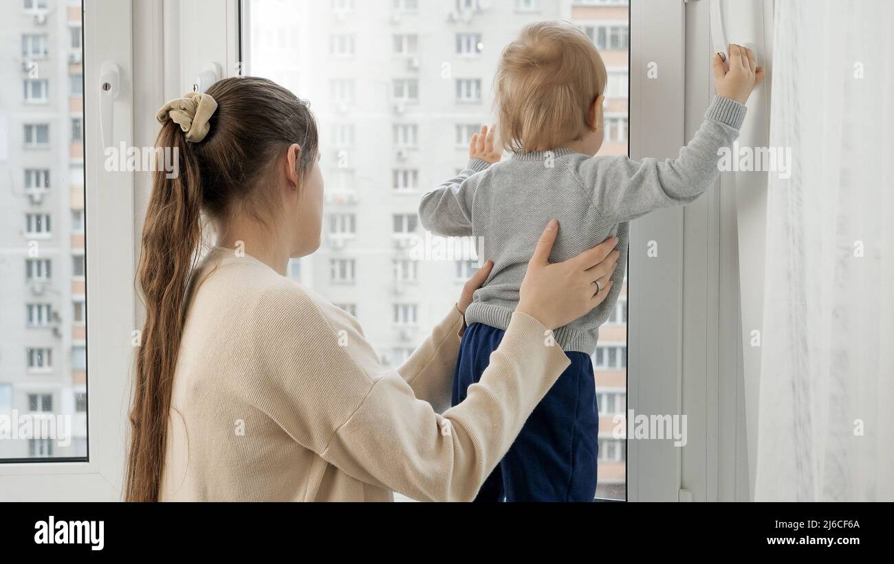 Little baby boy with mother looking out of the window of high store ...
