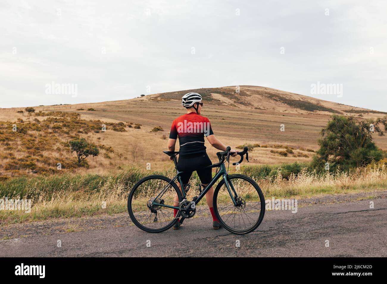 Back view of female cyclist taking break leaning on bike on empty ...
