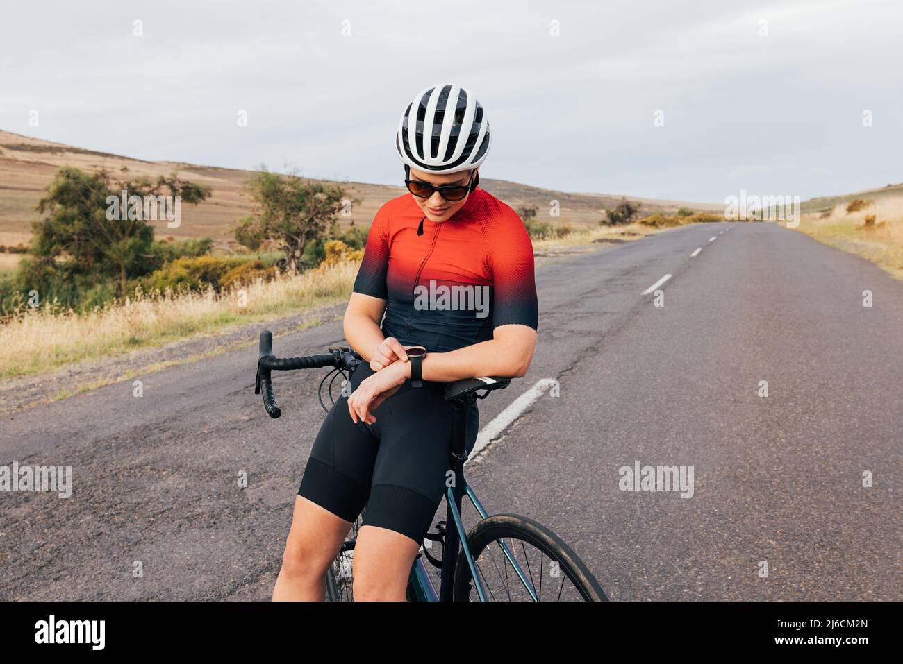 Woman cyclist in sportswear leaning on her bicycle checking smartwatch ...