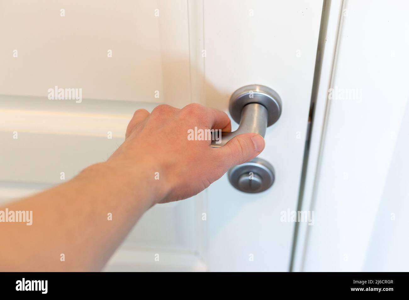 Hand presses the doorknob of a white door Stock Photo - Alamy