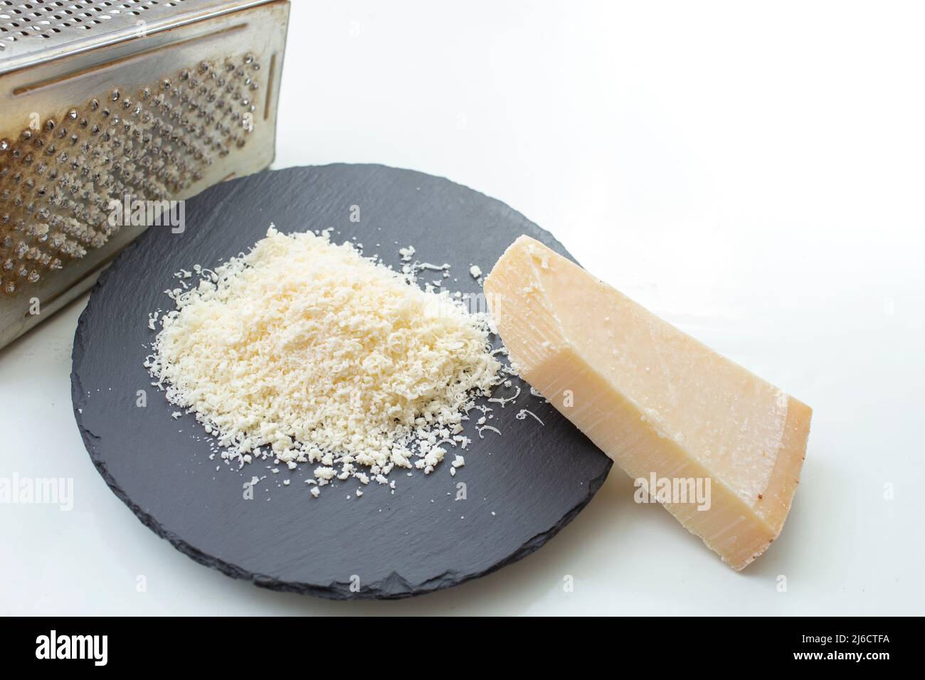grated parmesan on a black stone tile, isolated on white background ...