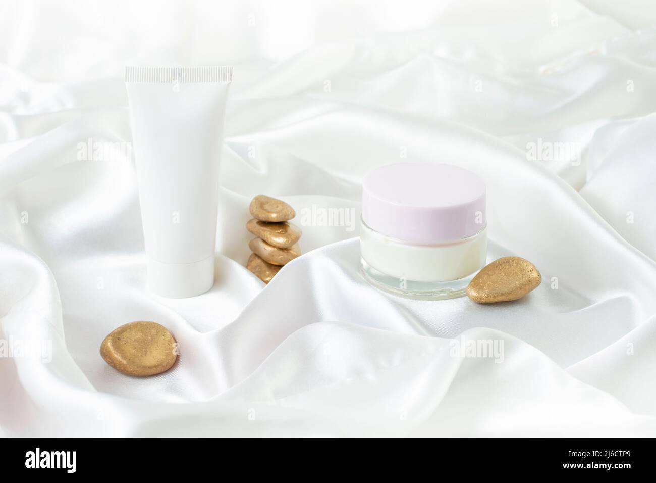 Hand cream tube and glass jar with empty space for label on white satin ...