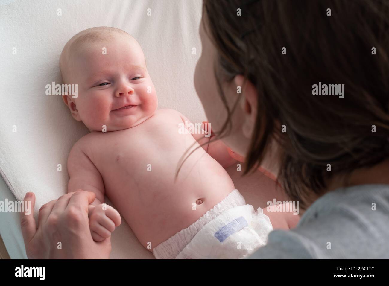 Caucasian baby looking on his mother smiling. Cuddling spending time ...