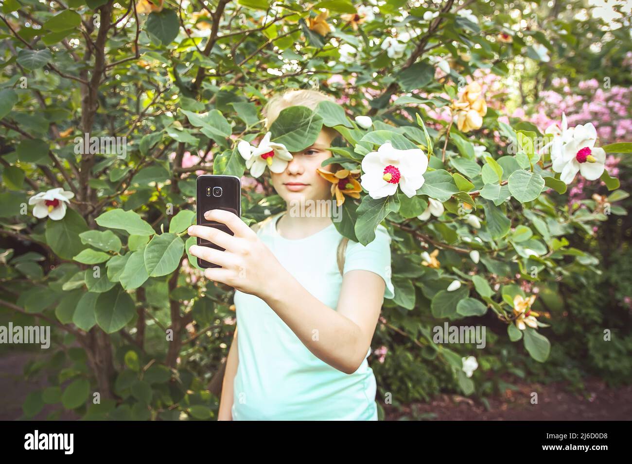 Beautiful teenager blonde girl make selfie on blooming spring magnolia ...