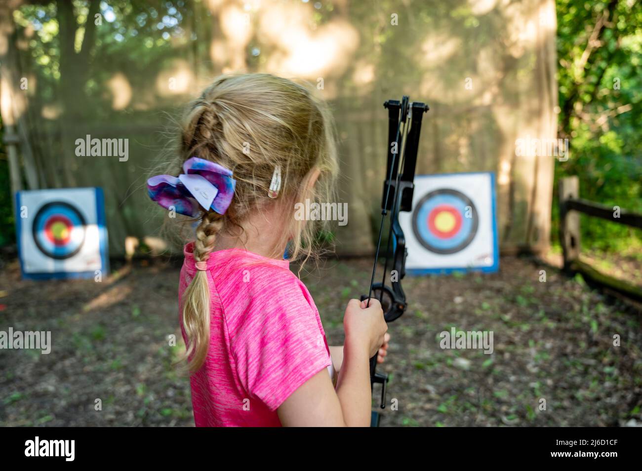Young girl at summer camp learning to use a bow and arrow looking down ...