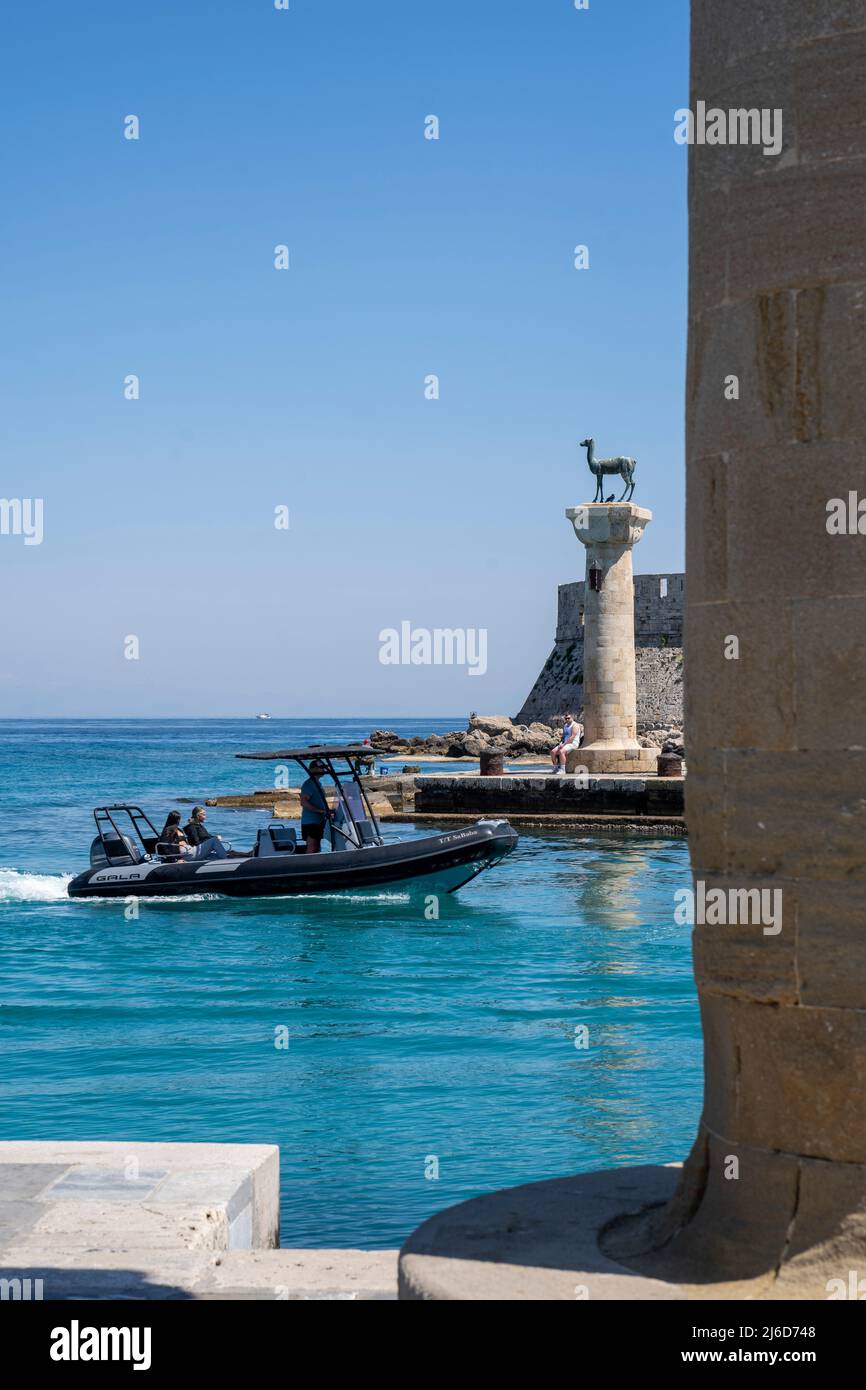 tourists boat sailing into Mandraki harbor passing the Doe statues in ...