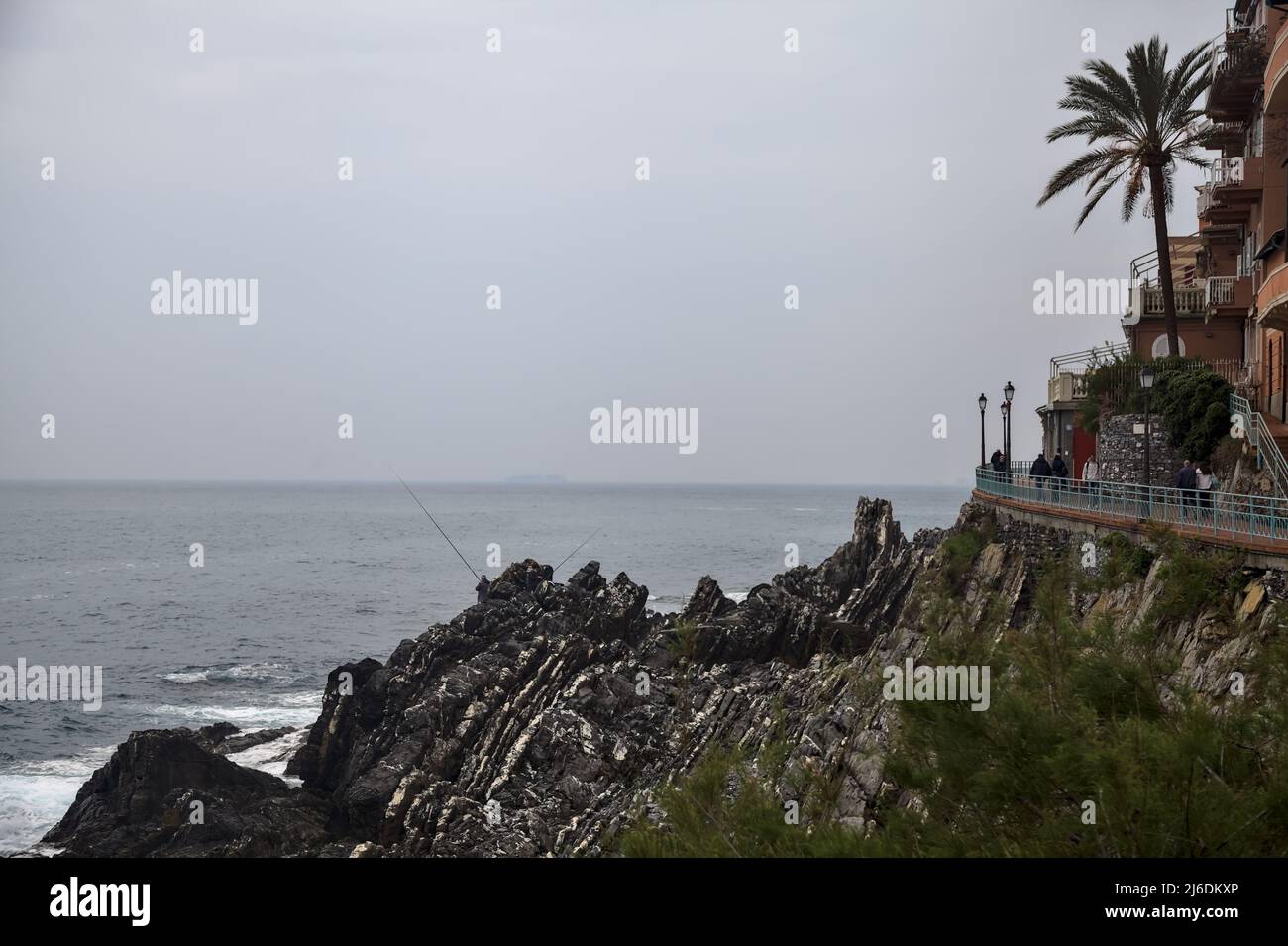 Paved trail on a cliff with buildings by the sea on a cloudy and rainy ...