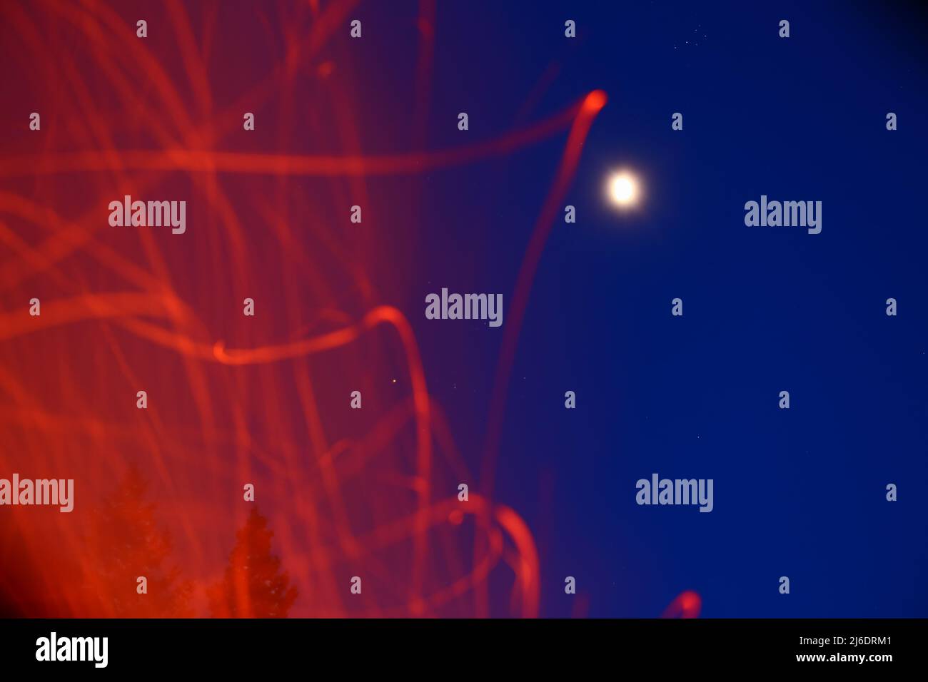 Trails of defocused sparks in front of sky with bright moon and stars ...