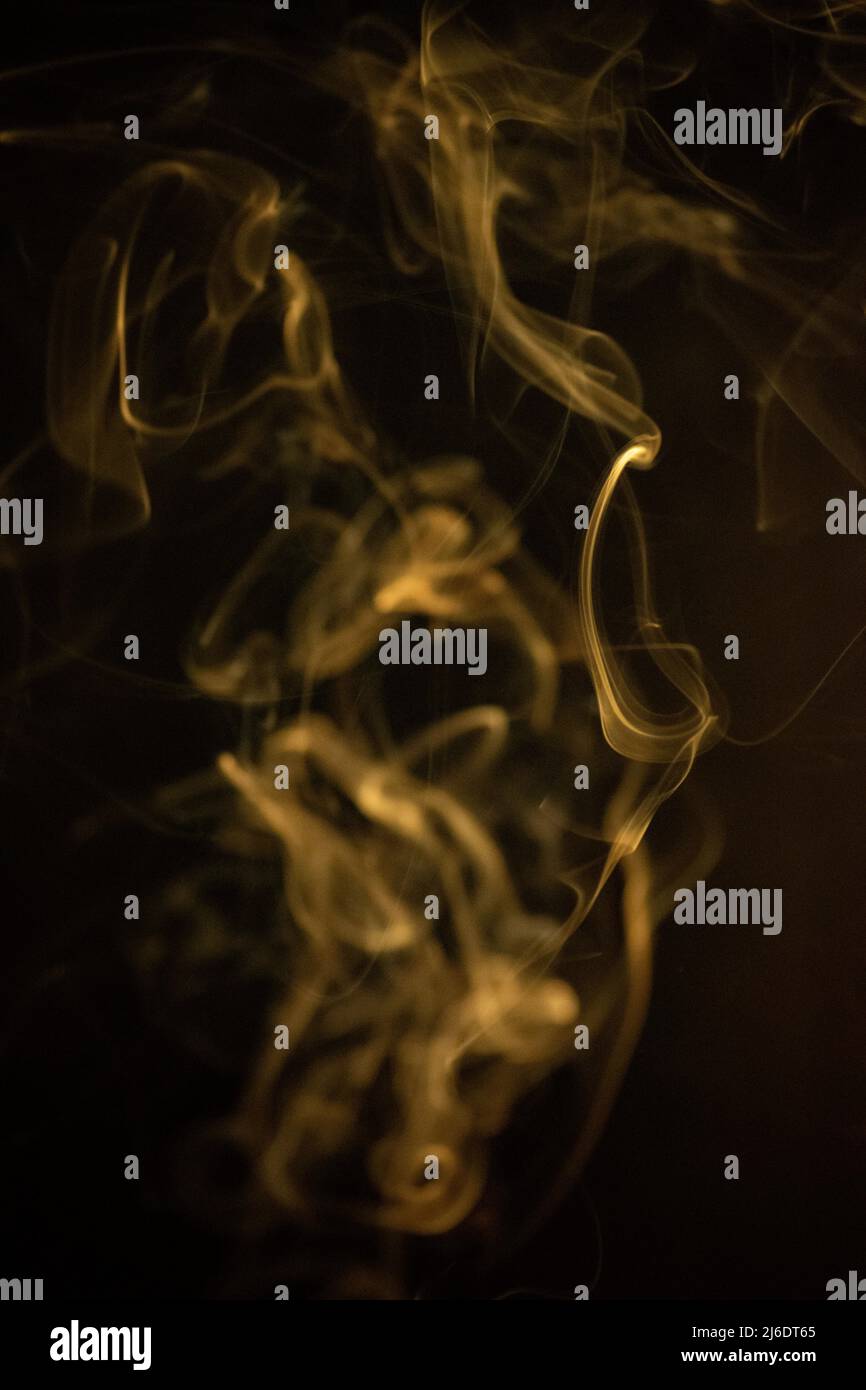 A yellow gold swirling, ascending smoke pattern on a black background ...
