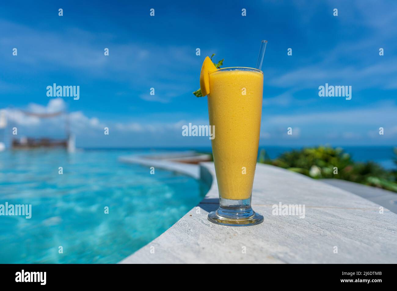 Glass of yellow mango smoothie on swimming pool and sea beach ...
