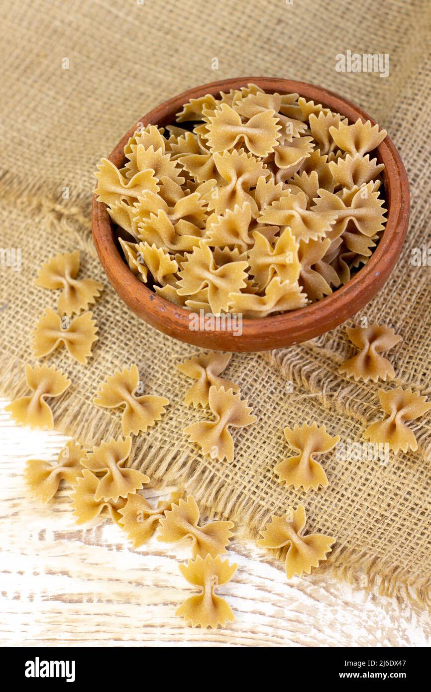 Whole grain dark pasta bows on brown plate on a rough wooden light ...