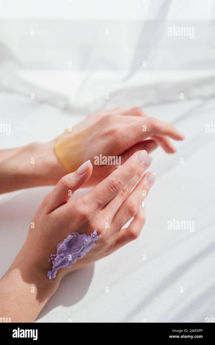 Female hands applying purple cream scrub on skin top view white ...