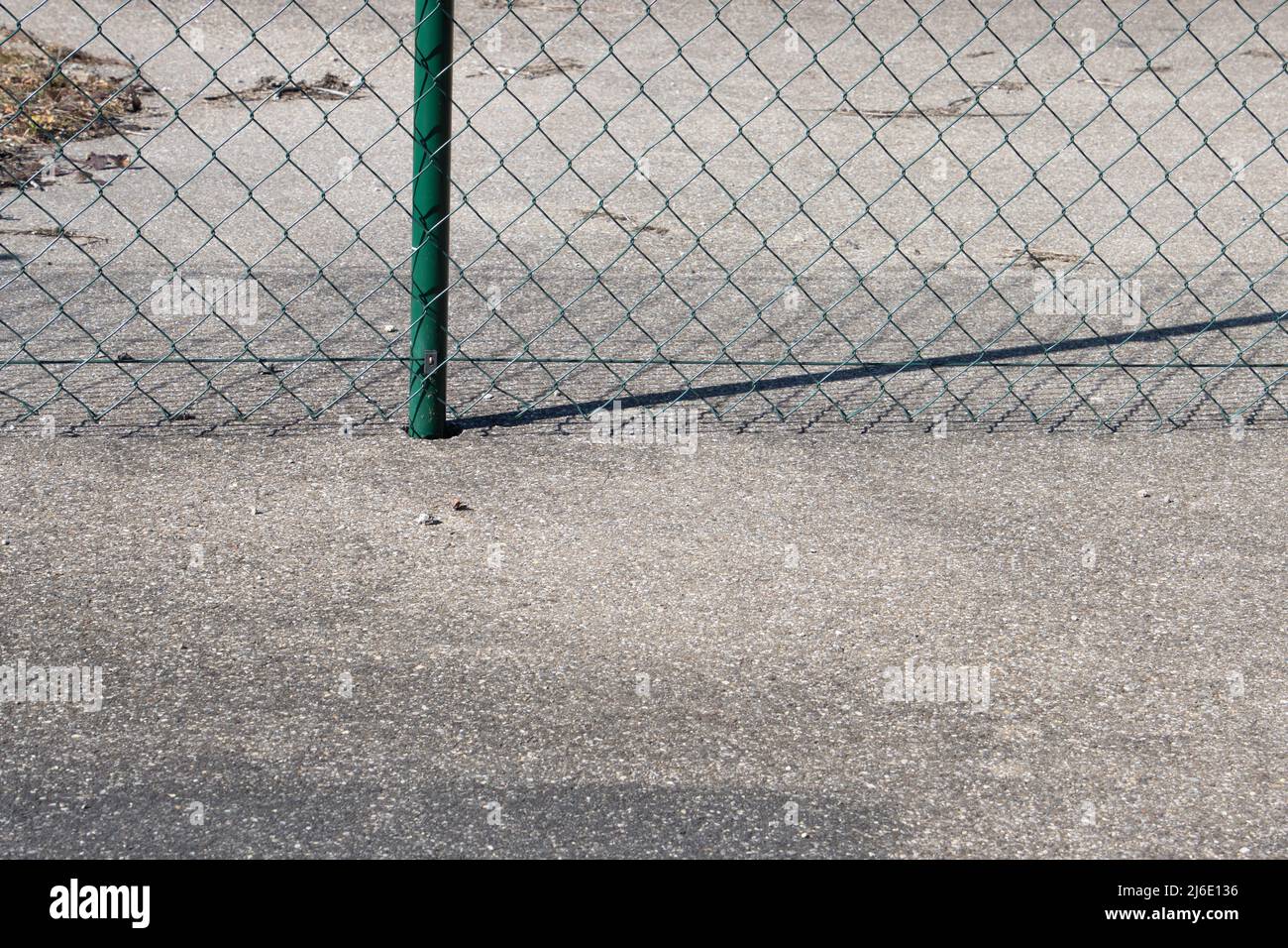 Green metal post concreted in a paved asphalt road with wire mesh fence ...