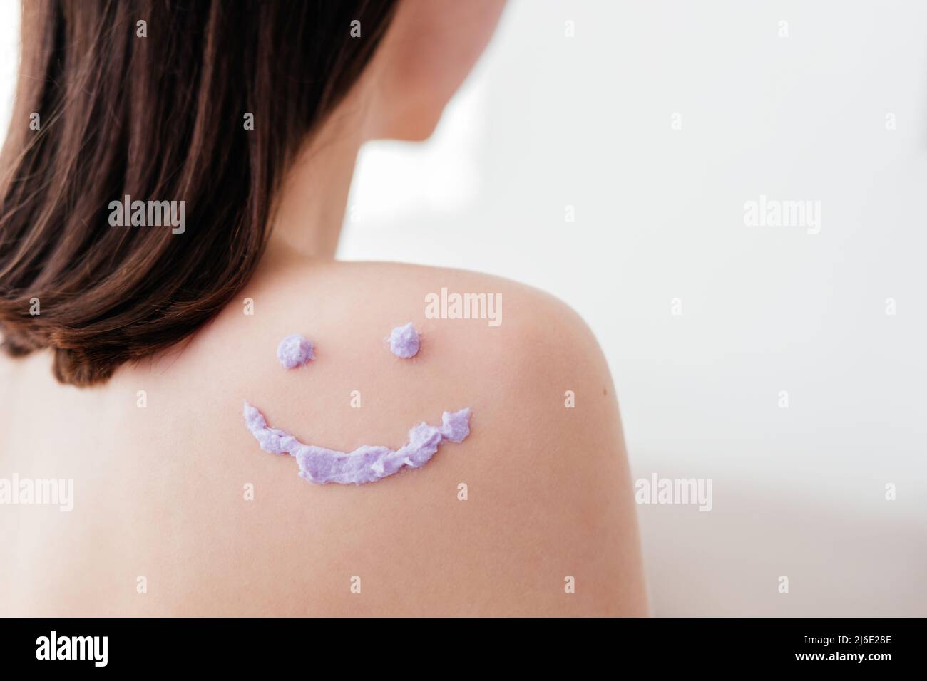 Smiley face made of purple cream scrub on shoulder of unrecognizable ...