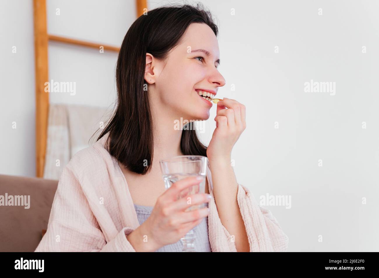 Smiling young woman holding pill omega capsule and glass of water ...