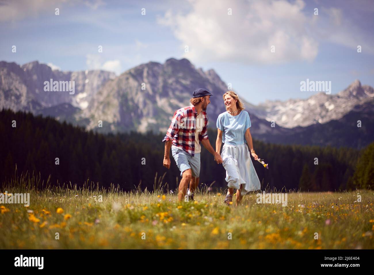 Smiling couple walking and holding hands in green meadow on sunny day ...