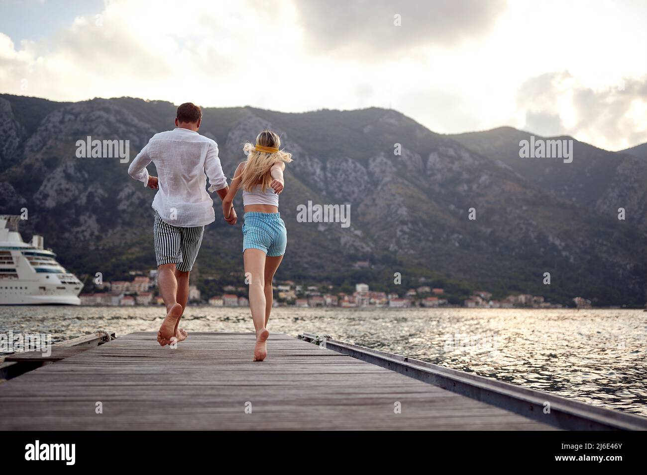 Rear view of romantic couple running on wooden dock holding hands ...