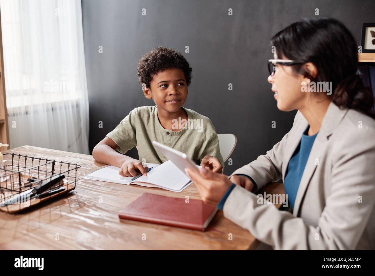 Young teacher using digital device while asking elementary student ... Young teacher using digital device while asking elementary student ...