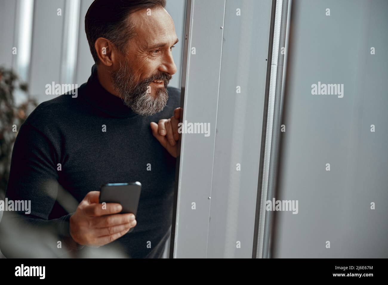 Smiling man with phone looking out the window Stock Photo - Alamy