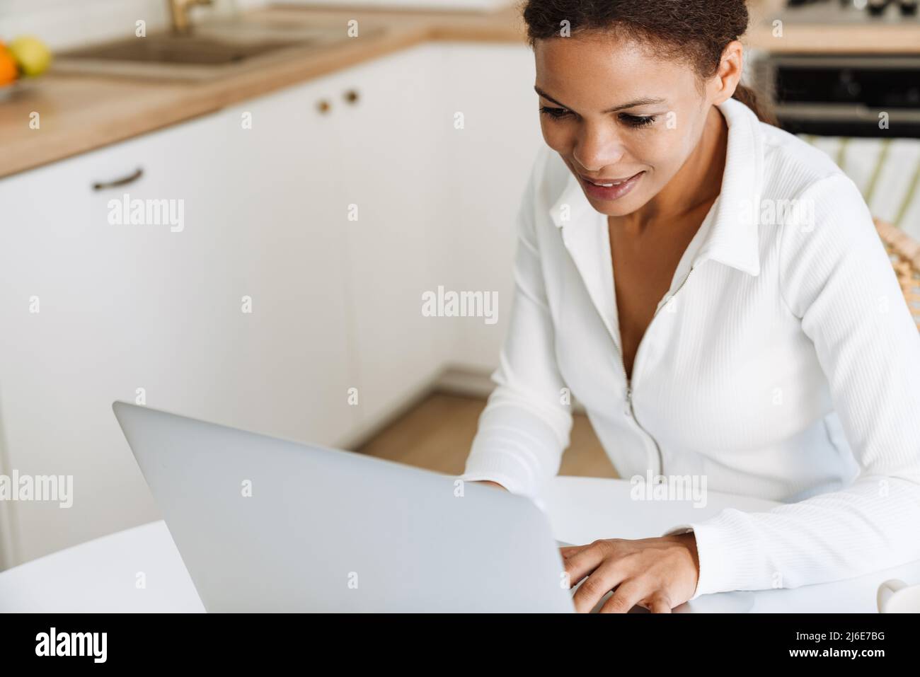 Black woman smiling while working with laptop in kitchen at home Stock ...