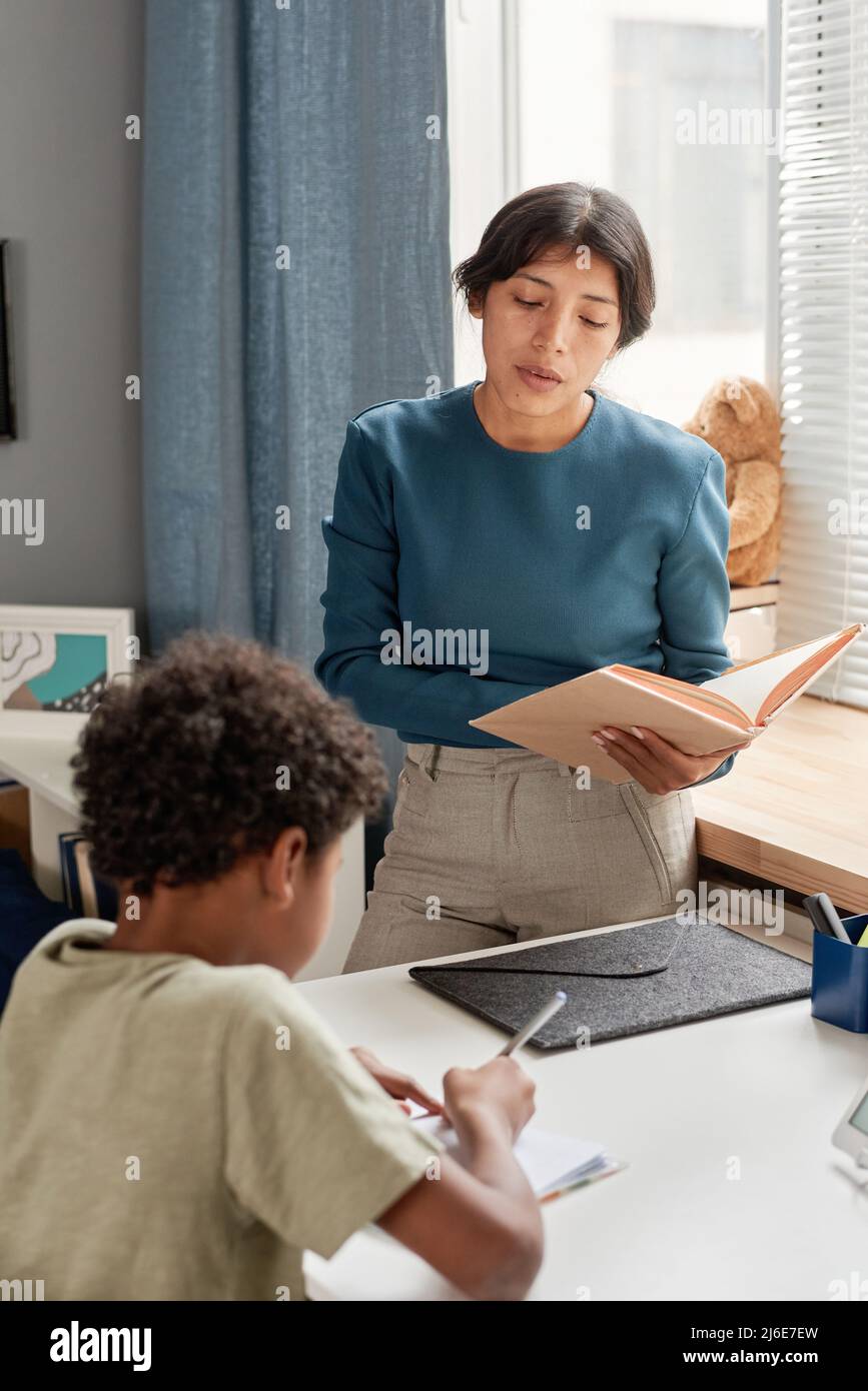 Young Latin tutor holding textbook while examining knowledges of her ...