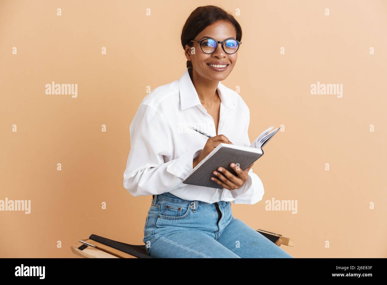 Young black woman writing down notes while sitting on chair isolated ...