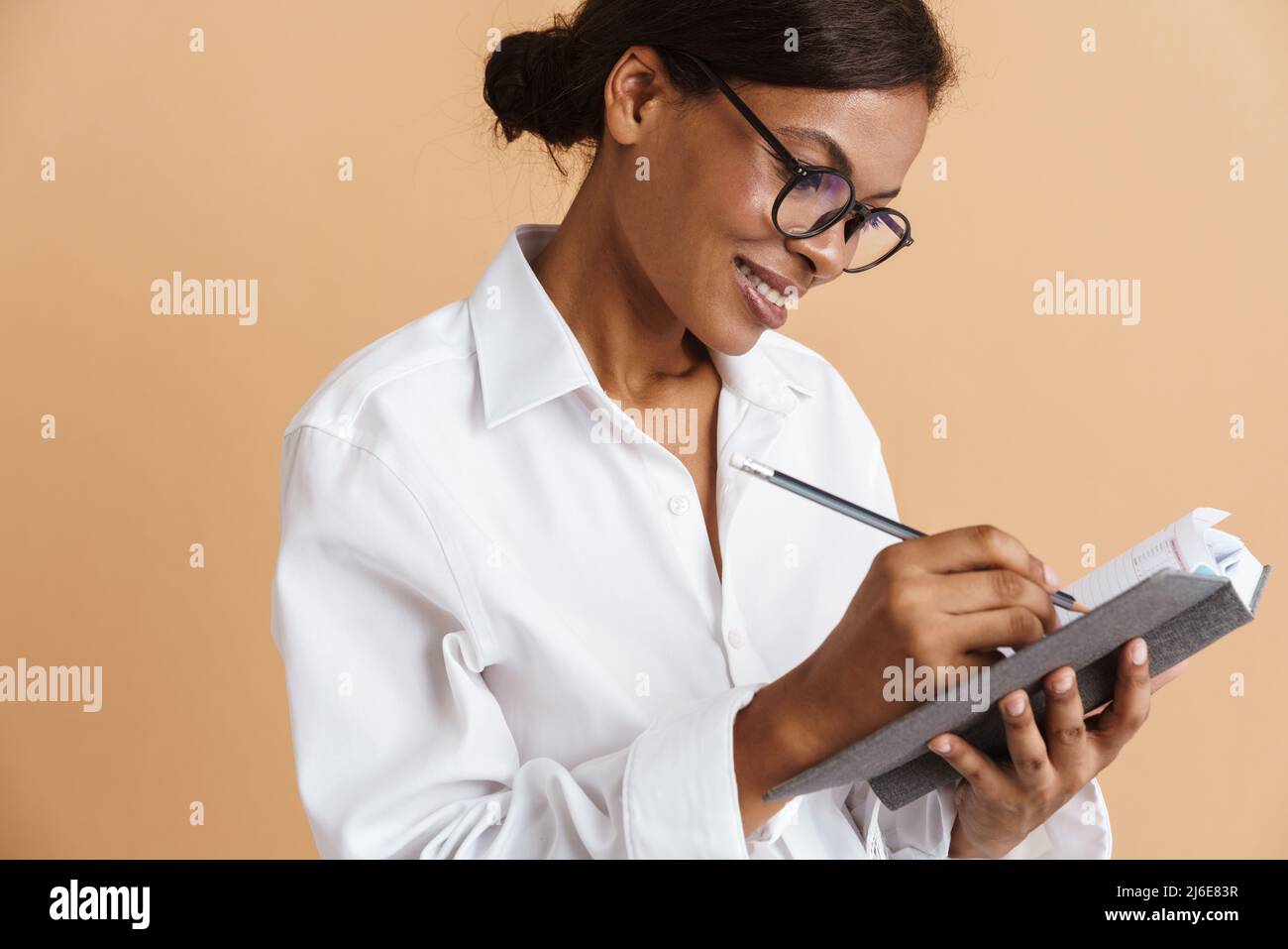 Young black woman wearing eyeglasses writing down notes in planner ...