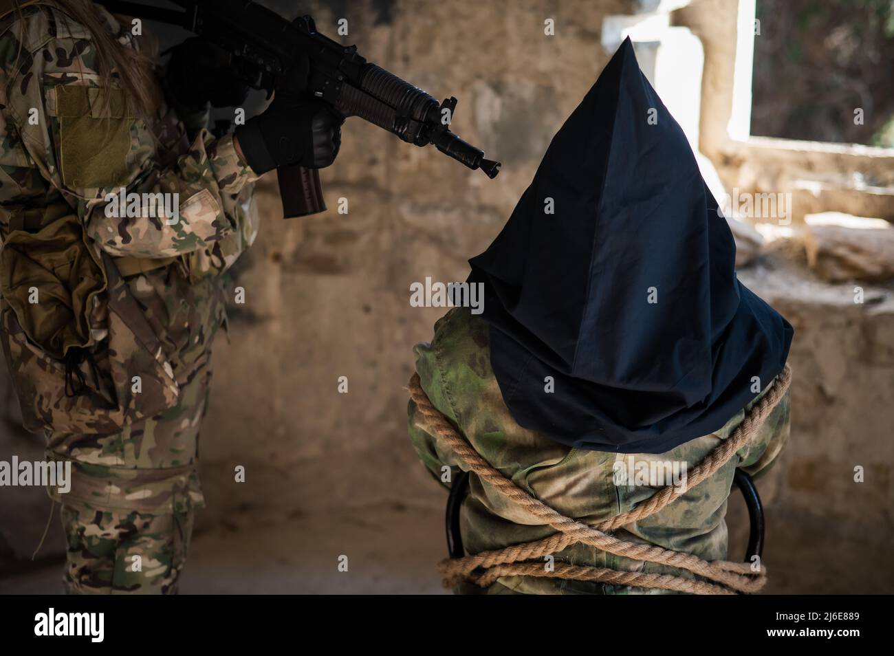 A caucasian woman in an army uniform holds a hostage with a bag on her ...