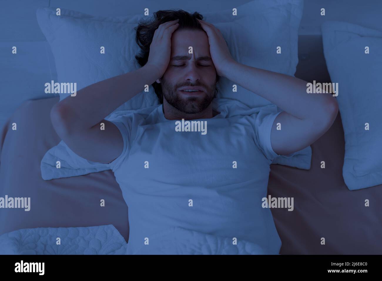 Sleepless guy laying alone in bed, touching his head Stock Photo - Alamy