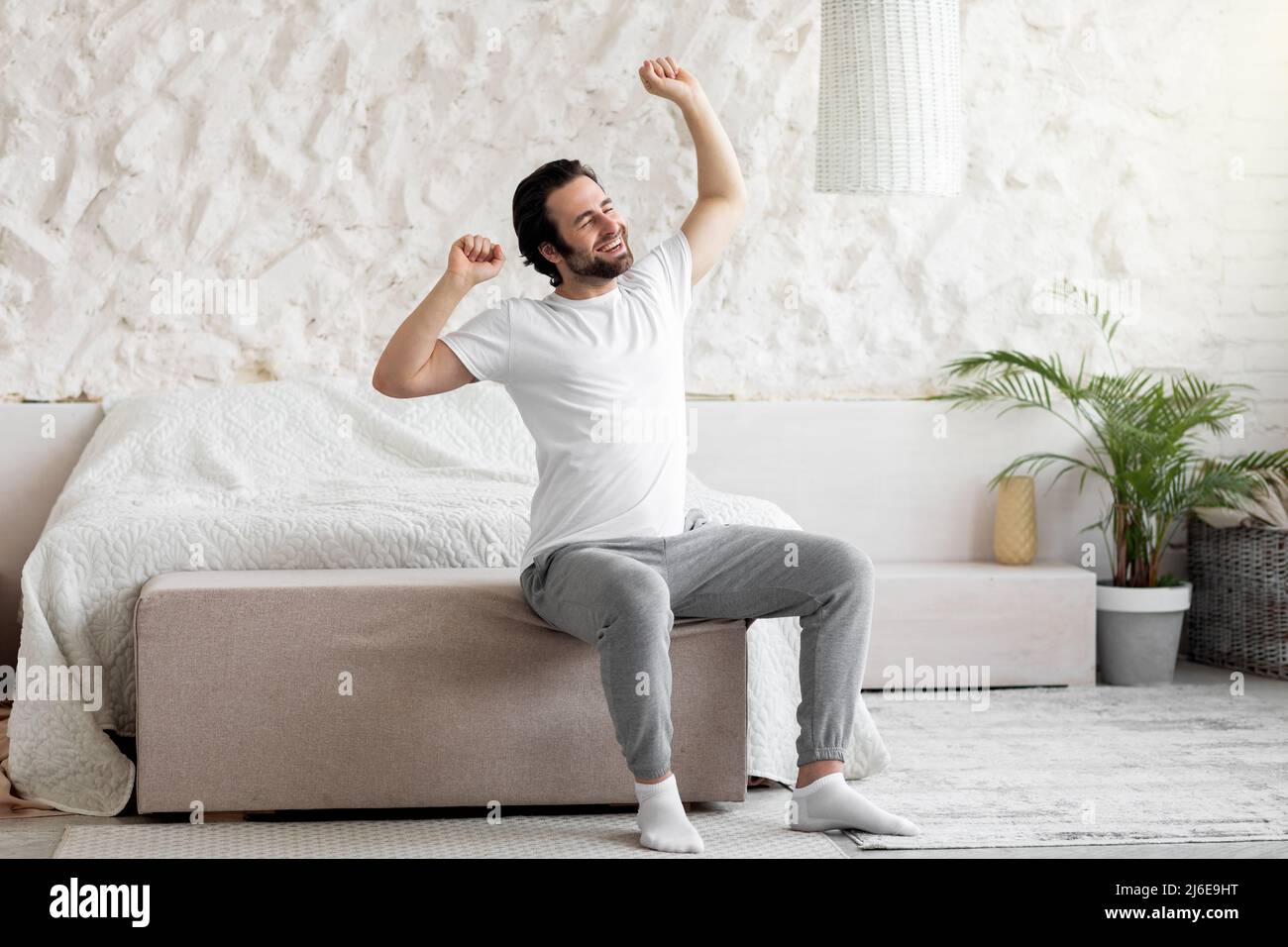 Young man waking up in bed and stretching his arms Stock Photo - Alamy
