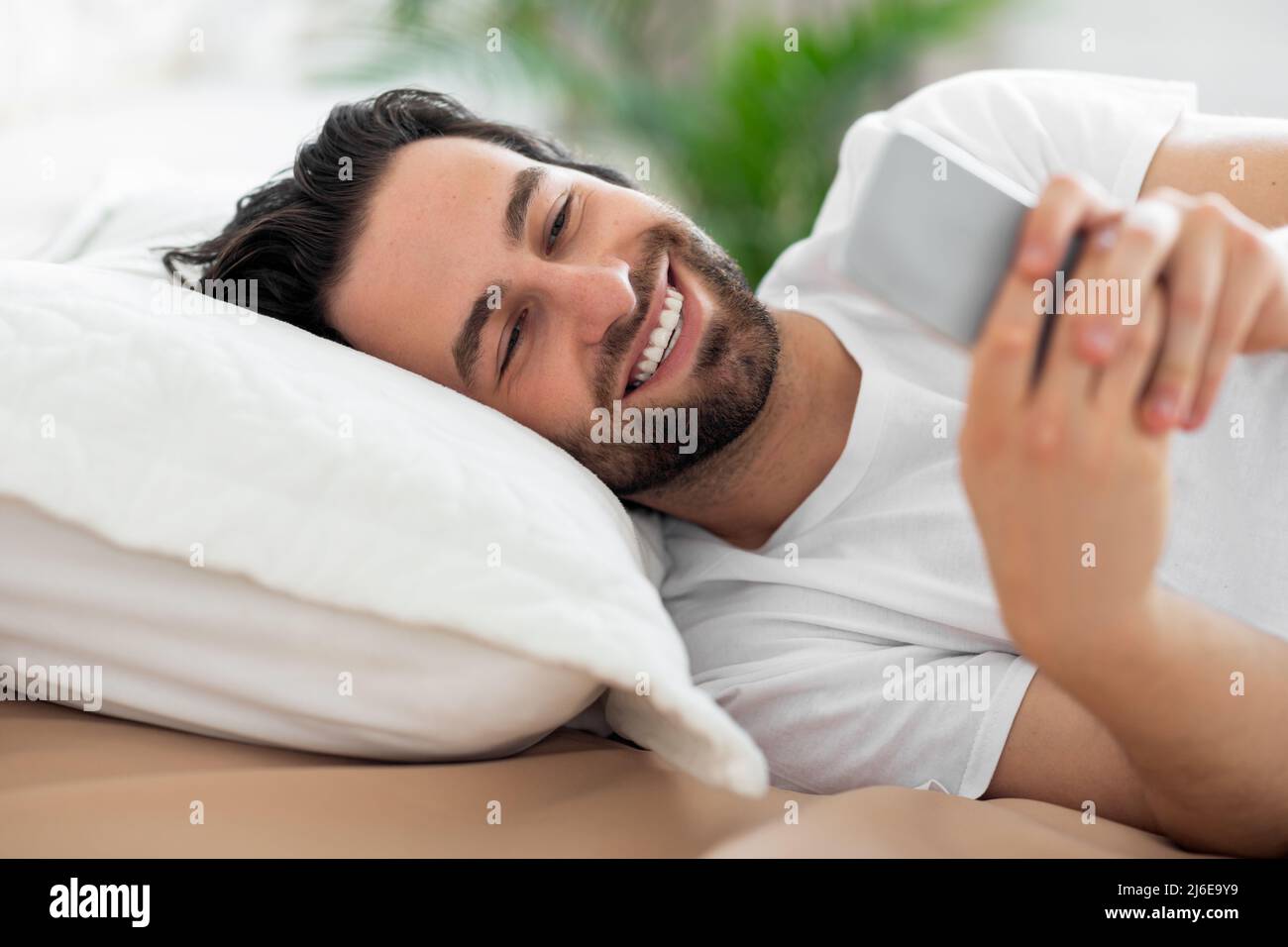 Relaxed guy chatting with friends on smartphone, lying on bed Stock ...
