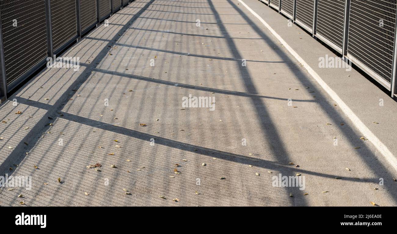 the metal railing of a pedestrian bridge casting shadows on the asphalt ...