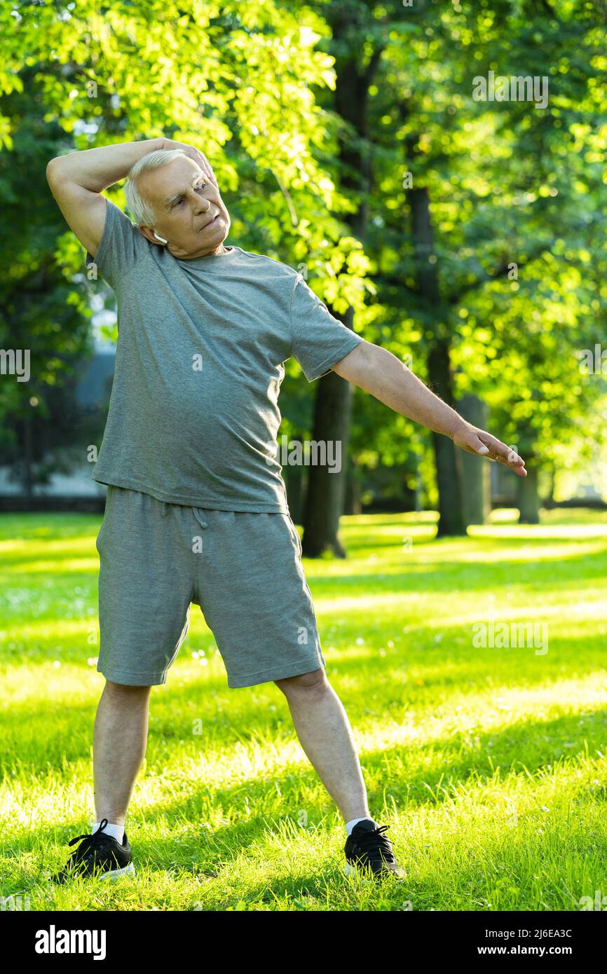 Elderly man exercising in green city park during his fitness workout ...
