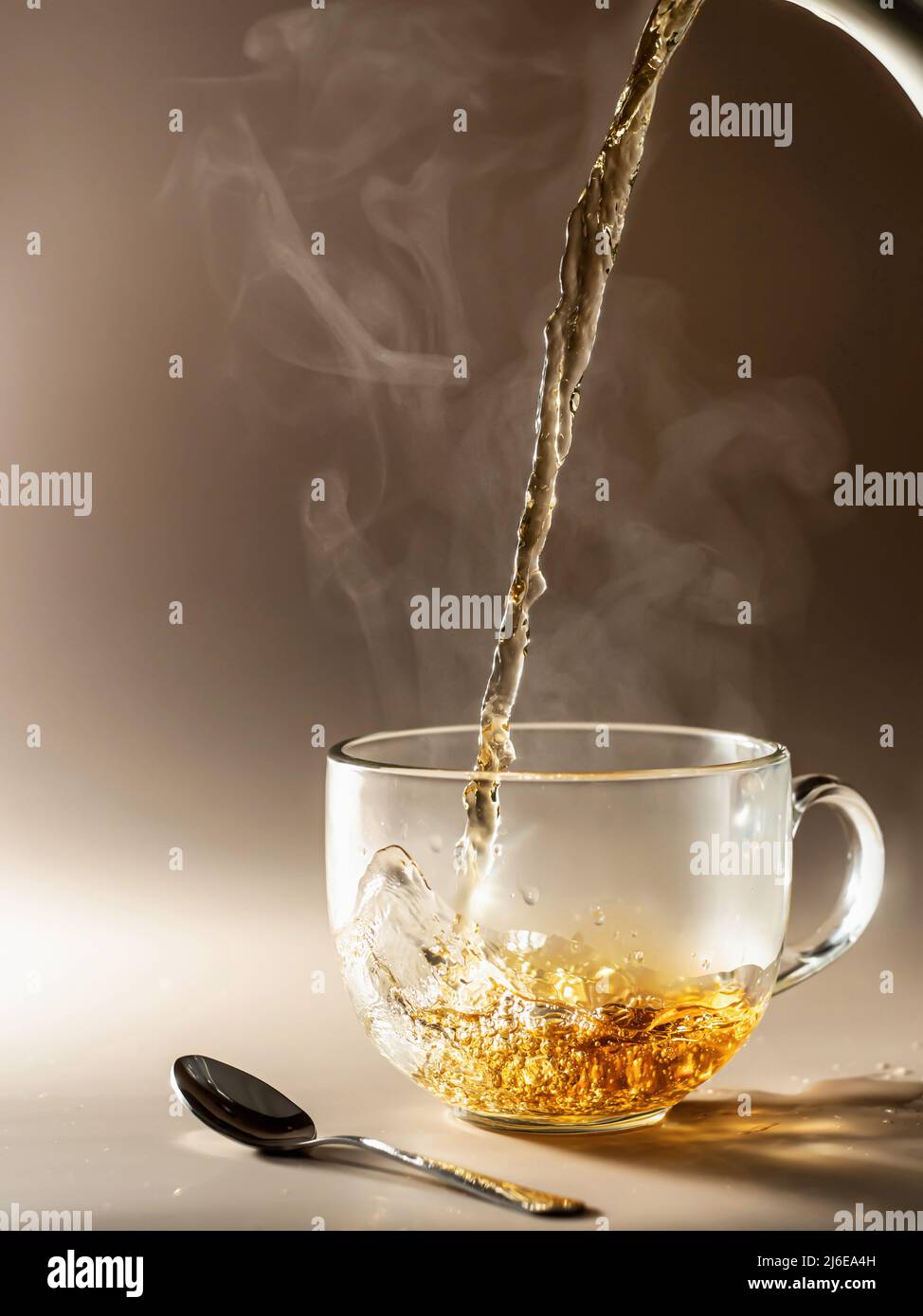 Tea being poured into glass tea cup on a brown monochrome background ...