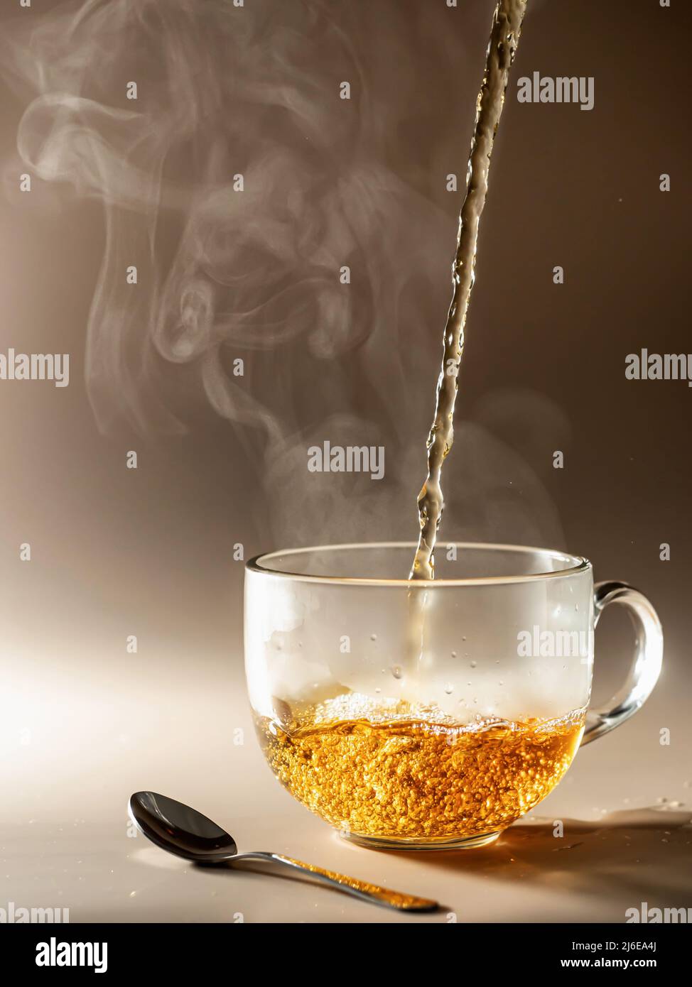 Tea being poured into glass tea cup with steam on brown monochrome ...