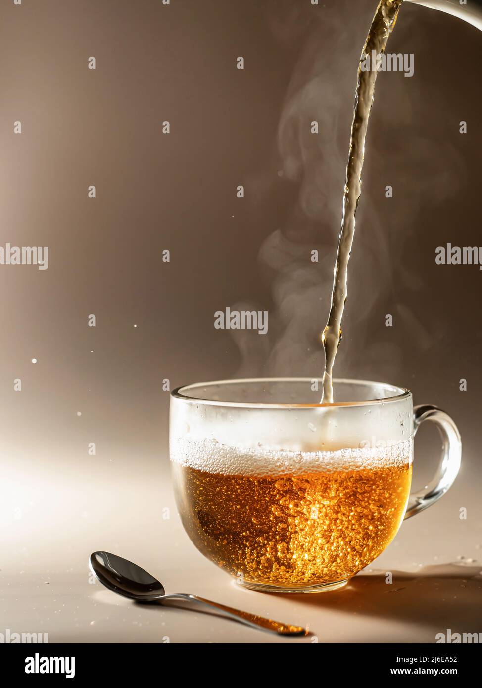 Tea being poured into glass tea cup on a brown monochrome background ...
