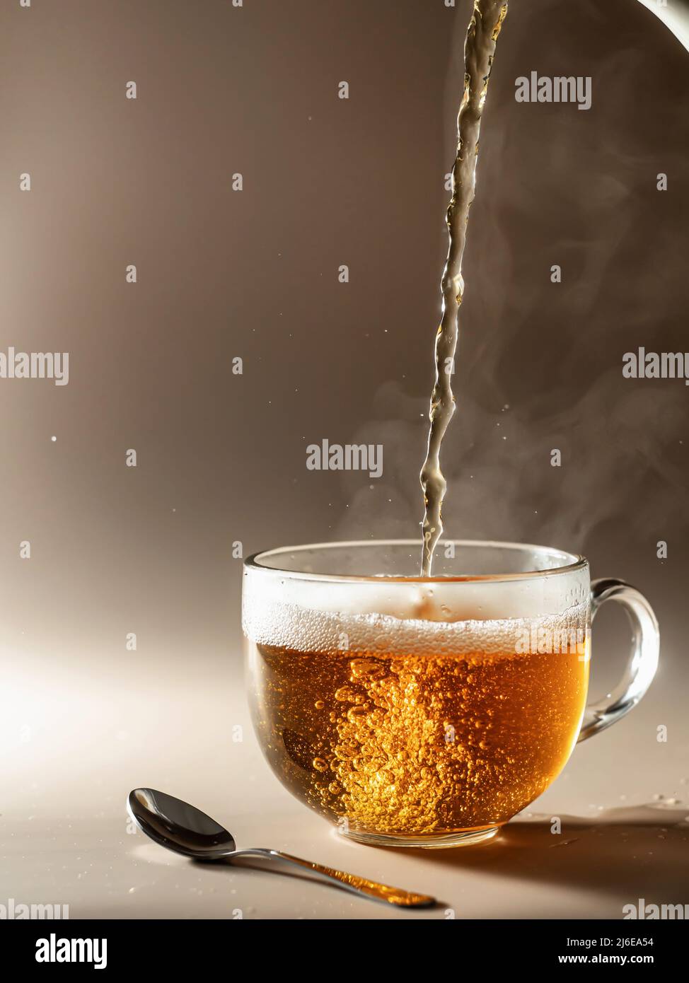 Tea being poured into glass tea cup with steam on brown monochrome ...