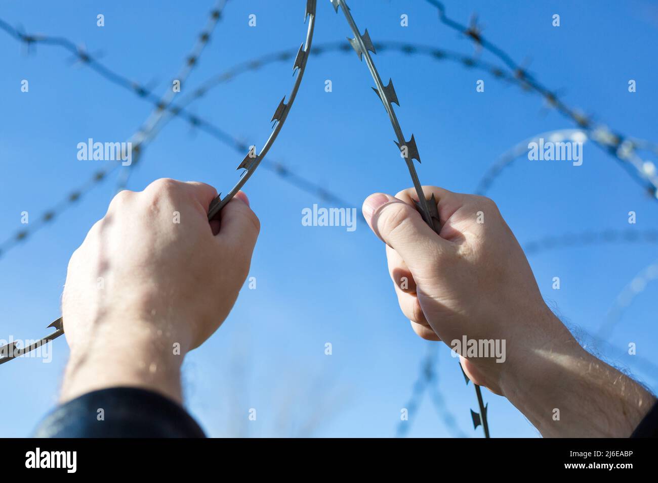 Men's hands tightly grip the barbed wire against blue sky, concept of ...