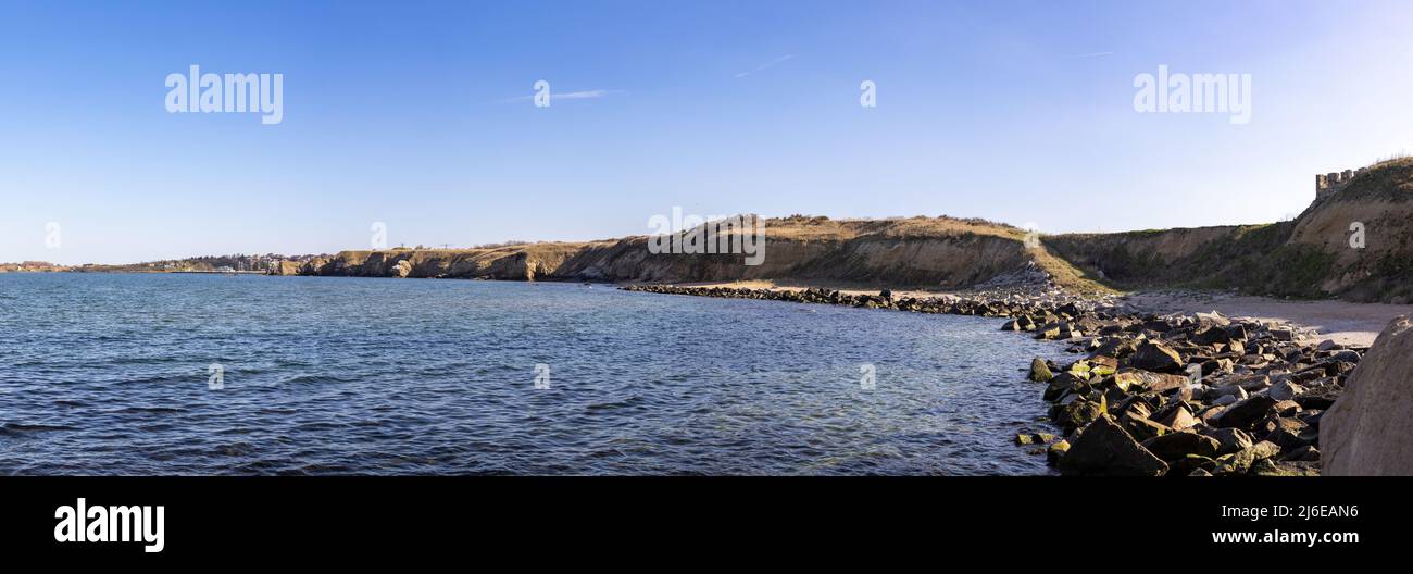 Panorama of a wild stone and sandy beach with dark wet sea sand and ...